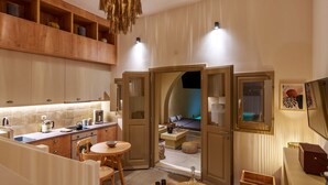 Uma cozinha moderna com armários de madeira, um espaço de refeições e uma porta aberta para uma sala de estar com sofá e televisão.