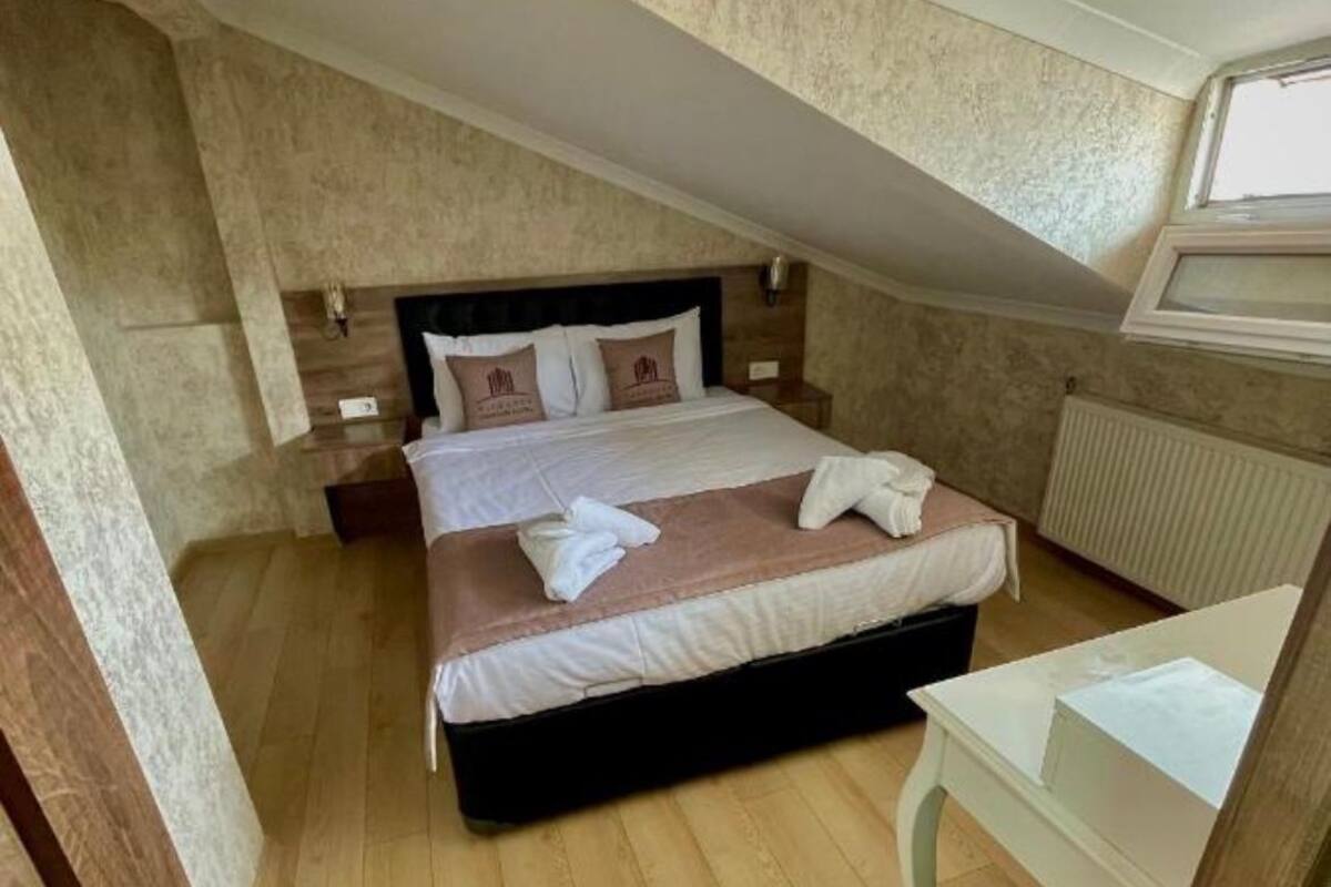Quarto com cama, mesas de cabeceira, uma mesinha e um radiador.