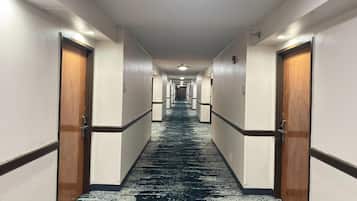 Corredor de hotel com portas em ambos os lados, piso coberto de carpete e iluminação embutida.