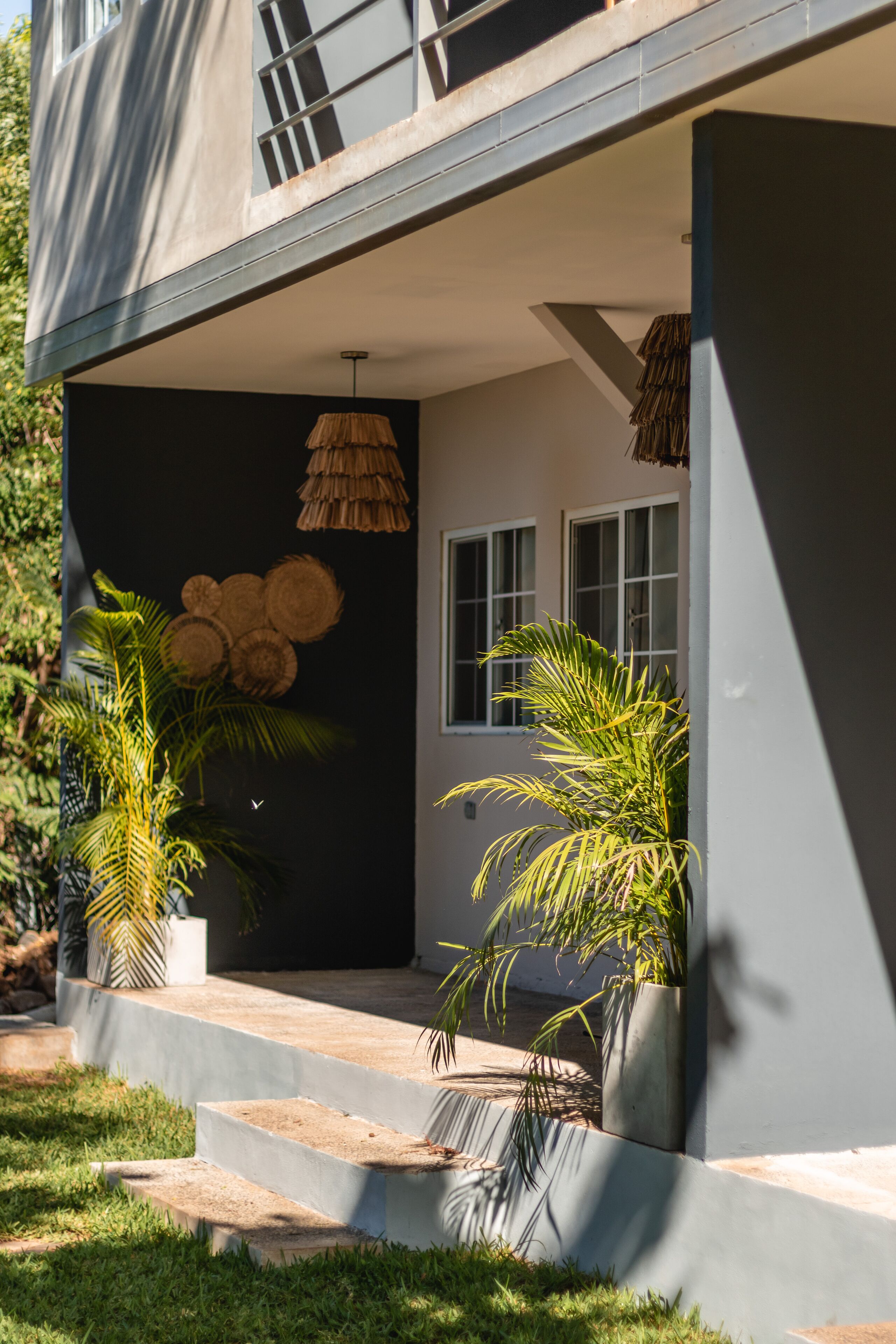 Uma casa moderna com varanda coberta, plantas em vasos e um lustre.