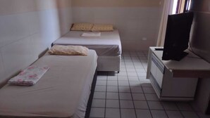Quarto pequeno e limpo com duas camas de solteiro, televisão de tela plana e uma mesinha.