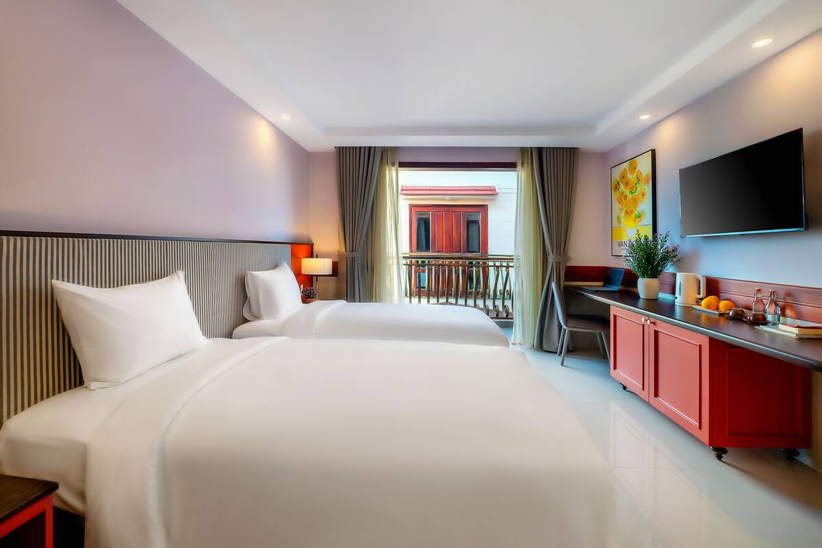 Quarto de hotel com duas camas, televisão, escrivaninha e varanda com vista.