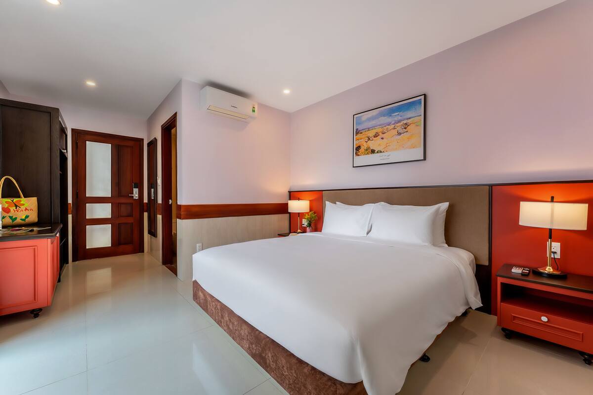 Quarto de hotel com uma cama grande, duas mesas de cabeceira com luminárias, um guarda-roupa, um espelho e um aparelho de ar condicionado.