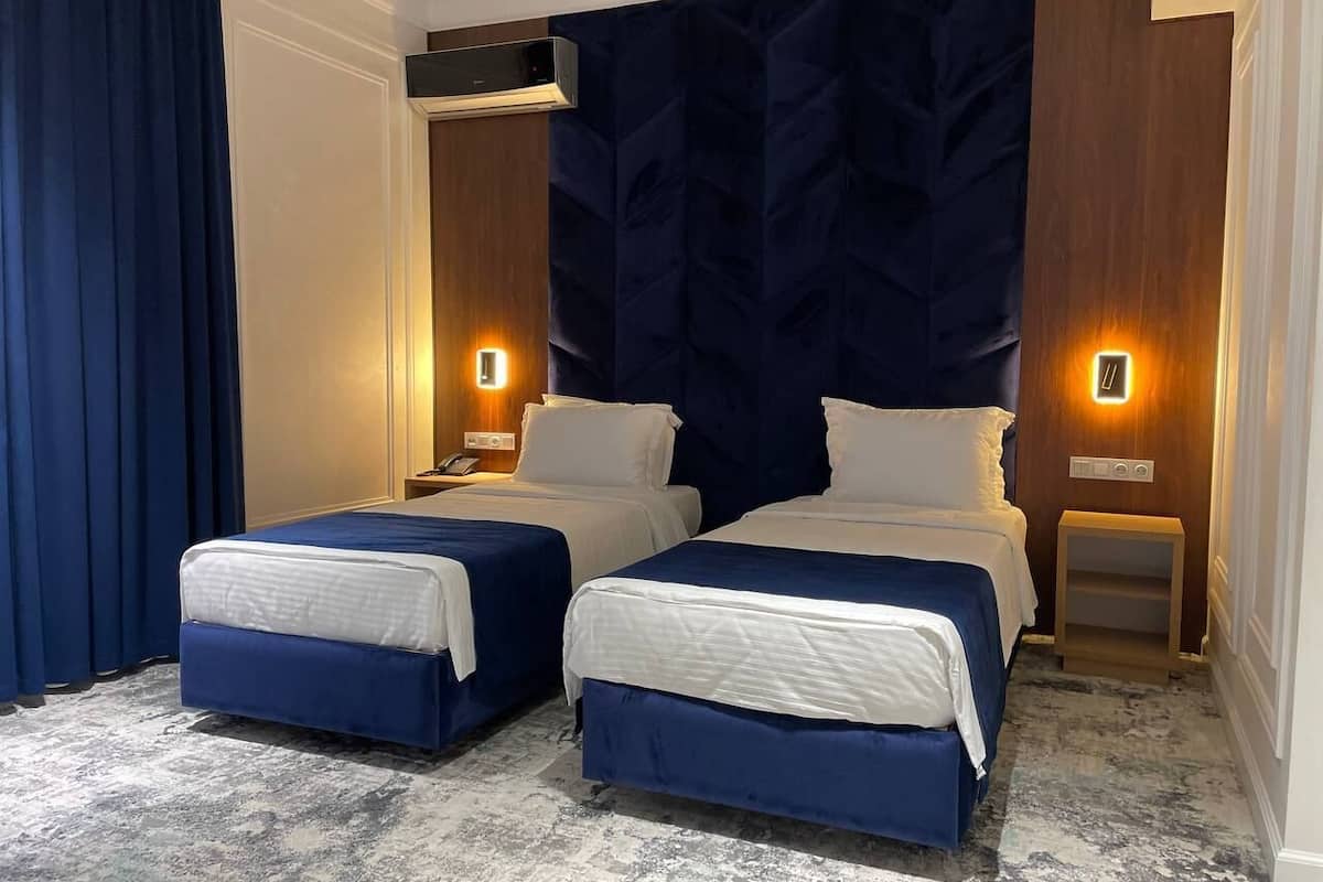 Quarto de hotel com duas camas, um espelho grande e cabeceira de madeira.