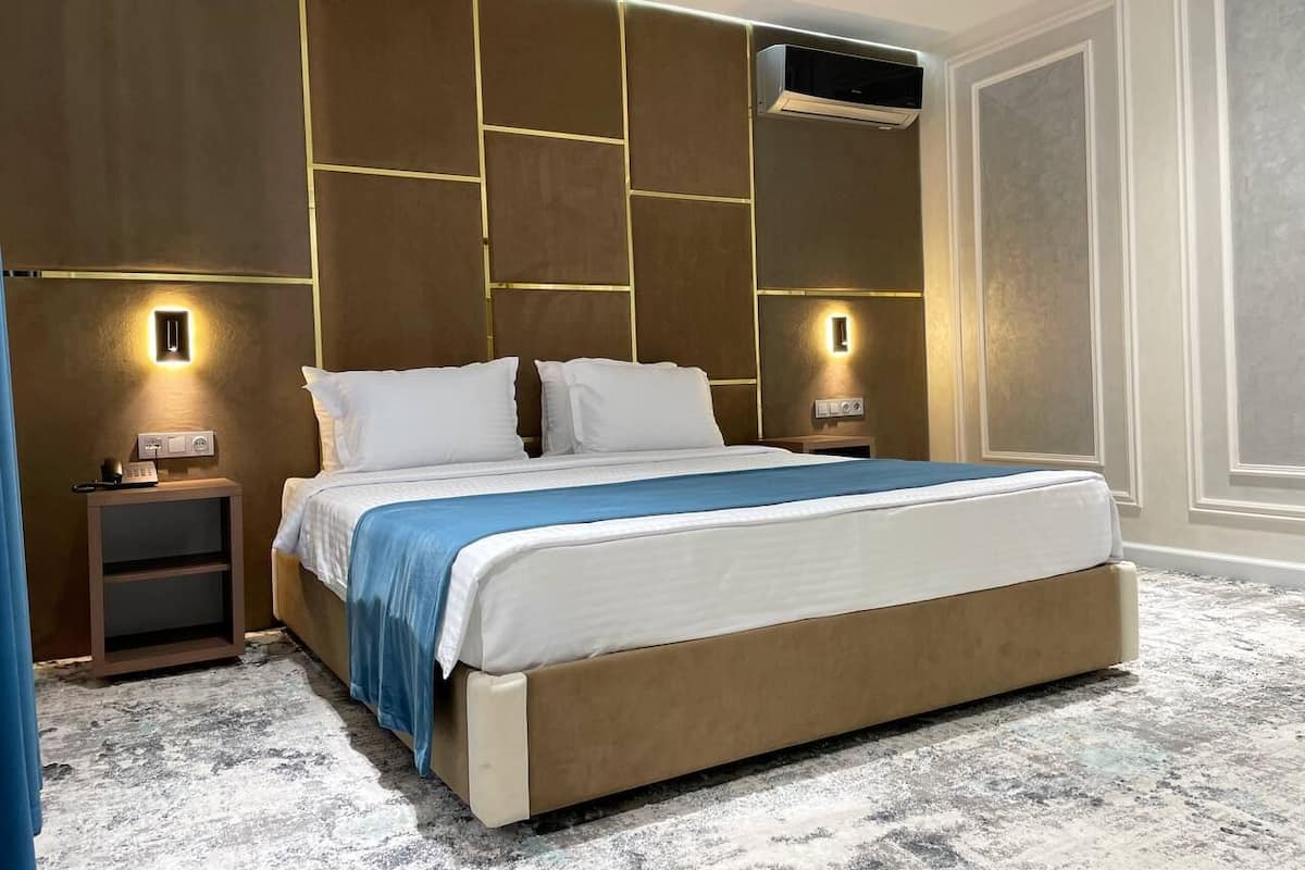 Quarto de hotel moderno com uma cama grande, mesas de cabeceira e iluminação embutida.