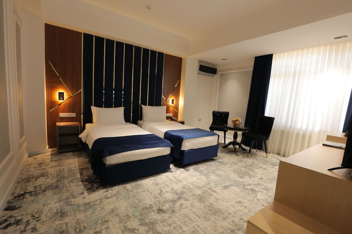 Quarto de hotel com duas camas, uma escrivaninha e uma cadeira.