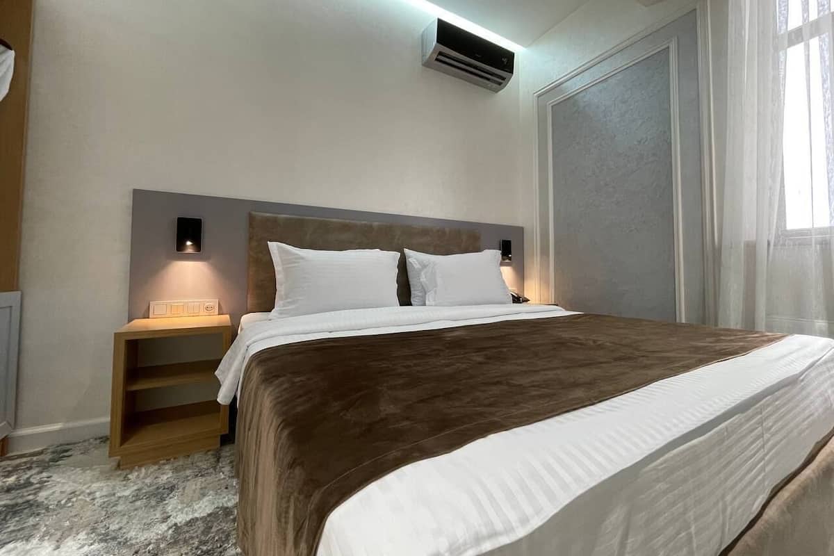 Uma cama bem arrumada com um cobertor marrom, uma mesa de cabeceira com abajur e um aparelho de ar condicionado na parede.