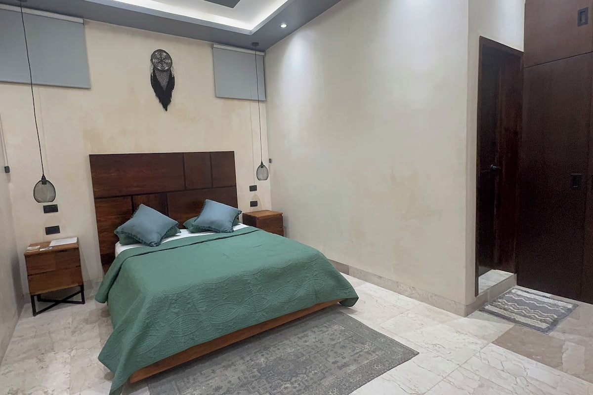 Um quarto com cama, mesas de cabeceira, cabeceira, um apanhador de sonhos e um guarda-roupa.