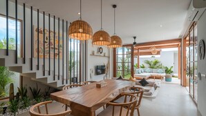 Um interior moderno com mesa de jantar de madeira, luminárias pendentes de vime e escada com corrimão preto.
