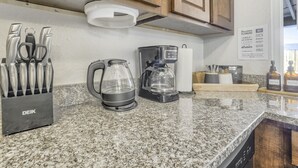 Cozinha com bancadas de granito, cafeteira, chaleira e porta-facas.