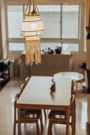 Uma área de refeições com mesa e cadeiras de madeira, luminária pendente e uma grande janela ao fundo.