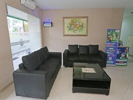 Uma sala de estar com dois sofás pretos, uma mesa de centro de vidro e um quadro floral emoldurado na parede.