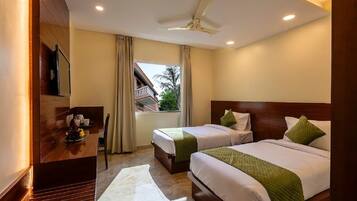 Quarto de hotel com duas camas, uma escrivaninha com cadeira, um ventilador de teto e uma janela com cortinas.