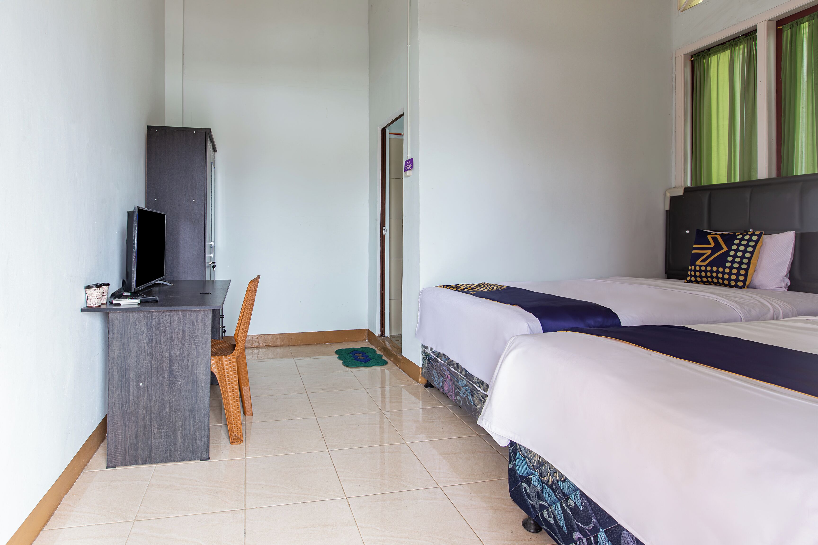Quarto de hotel com escrivaninha, duas camas, uma cadeira e uma porta.
