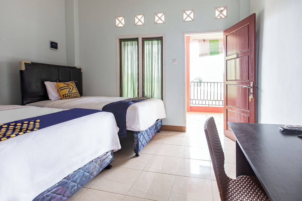 Quarto de hotel com duas camas, uma mesa de jantar e vista para o exterior através de uma porta.
