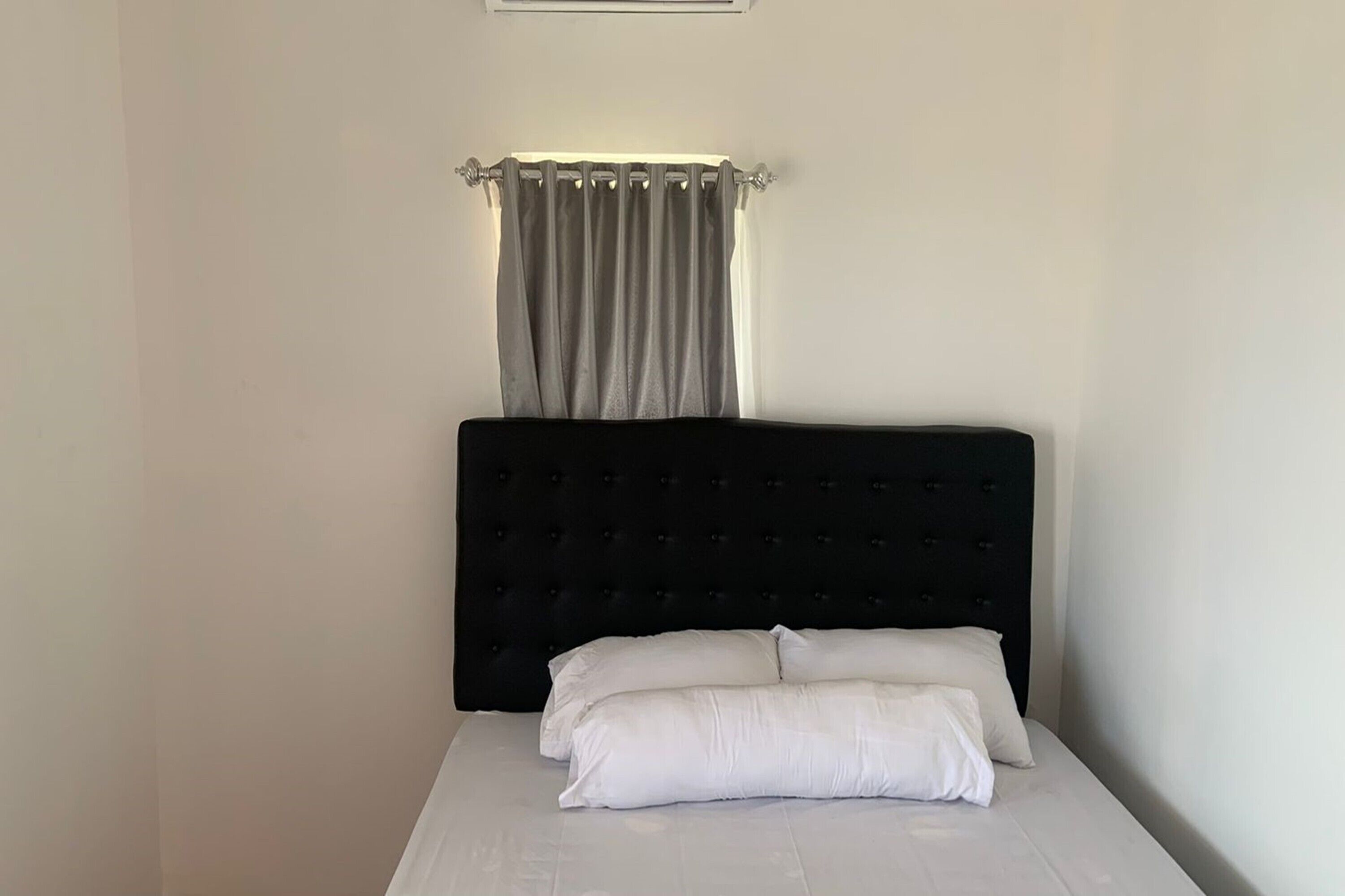 Quarto com cabeceira estofada preta, colchão branco e cortina cinza.
