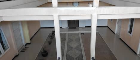 Um edifício com vários níveis, espaço aberto central, guarda-corpos e plantas em vasos.
