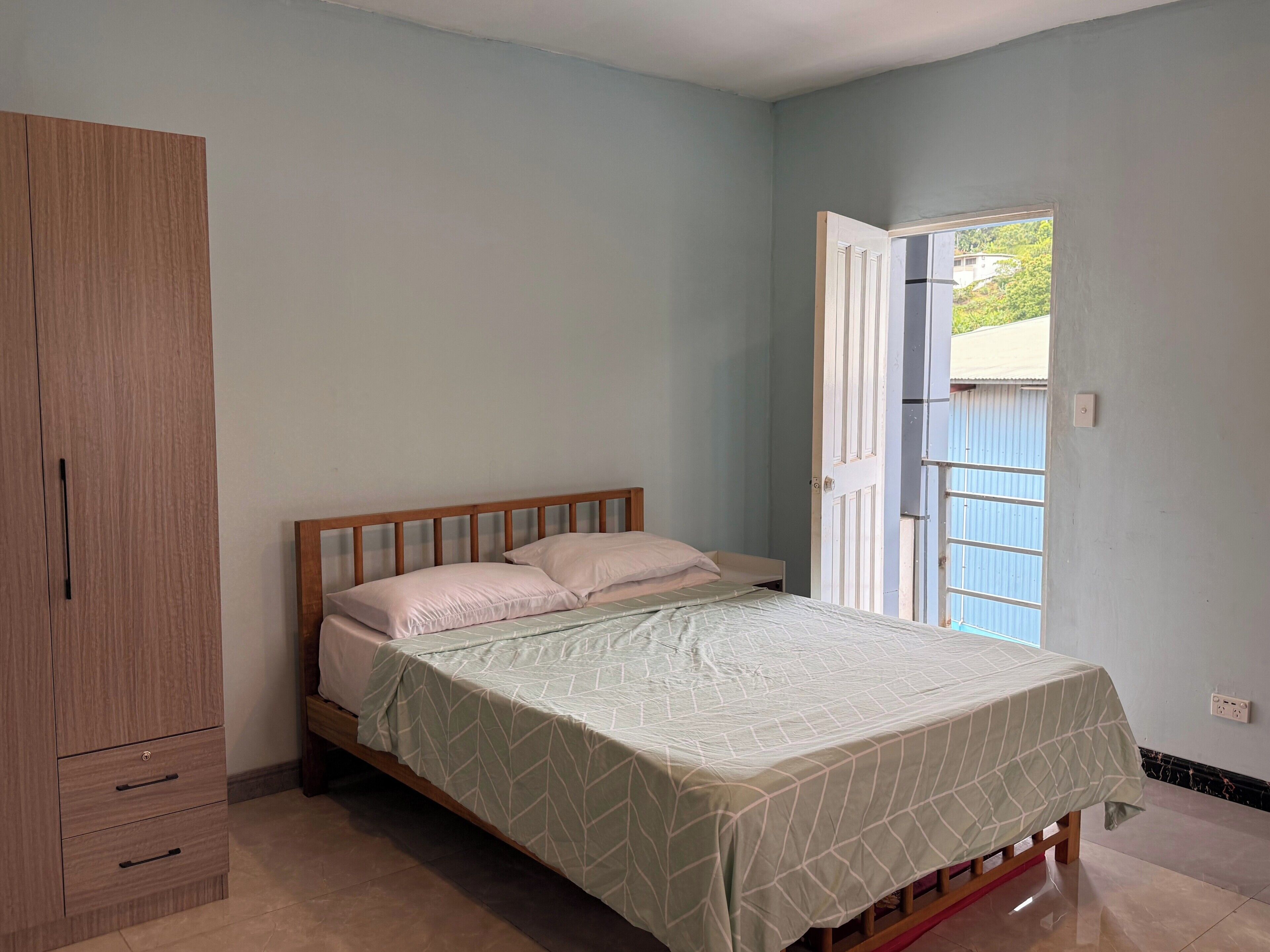 Quarto com cama, guarda-roupa e porta aberta para o exterior.