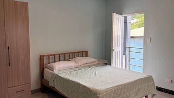 Quarto com cama, guarda-roupa e porta aberta para o exterior.