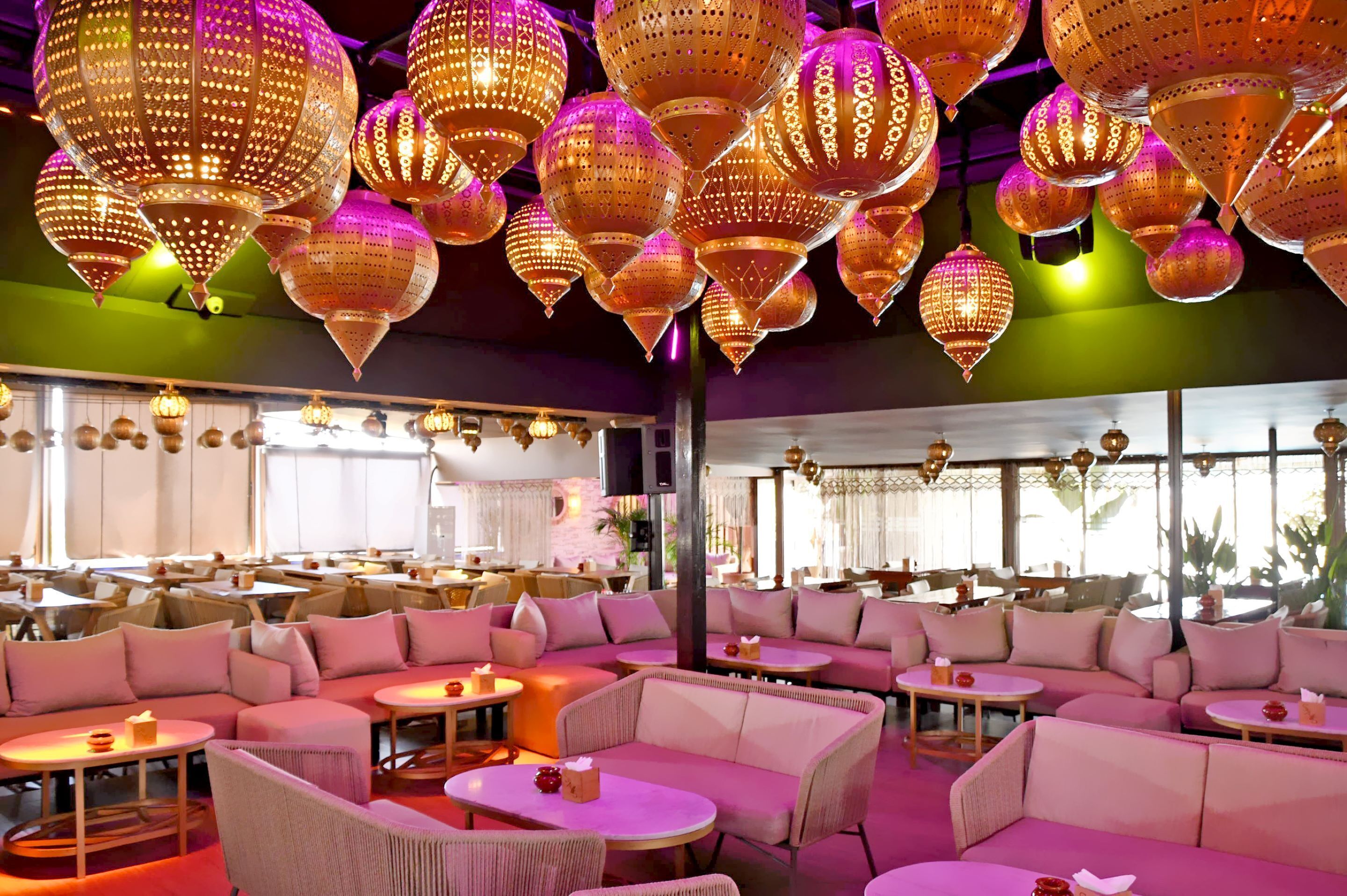 Restaurante com várias áreas de estar, incluindo sofás e mesas redondas, e lanternas decorativas penduradas.