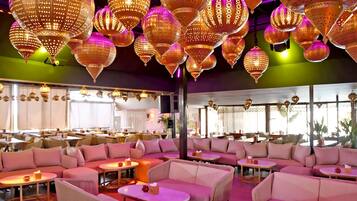 Restaurante com várias áreas de estar, incluindo sofás e mesas redondas, e lanternas decorativas penduradas.