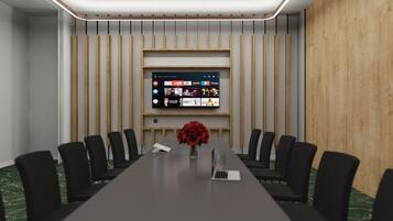 Uma sala de conferências com uma mesa comprida, cadeiras pretas, uma peça central florida e uma TV montada exibindo serviços de streaming.