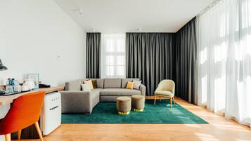 Uma sala de estar moderna com um sofá seccional cinza, uma mesa redonda pequena, uma cadeira vermelha, um mini-refrigerador branco e um tapete verde.