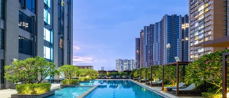 Piscina com espreguiçadeiras e vegetação, cercada por edifícios altos.