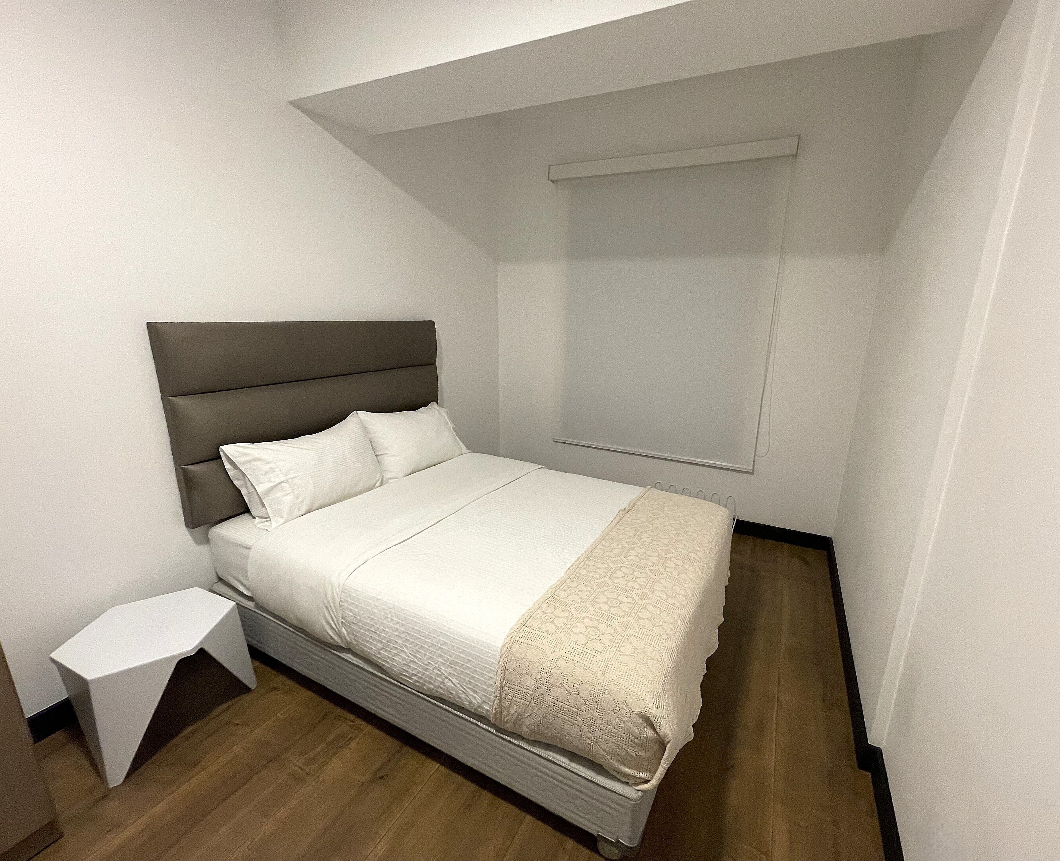 Quarto com cama, mesa de cabeceira e janela.