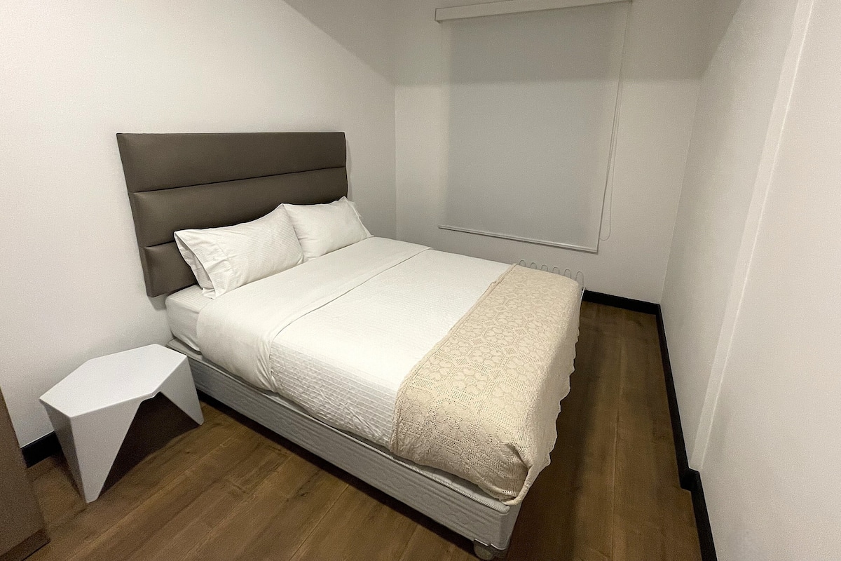 Quarto com cama, mesa de cabeceira e janela.