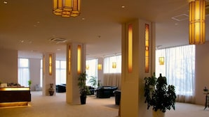 Um hall amplo com balcão de recepção, área de estar e grandes janelas que proporcionam iluminação natural.