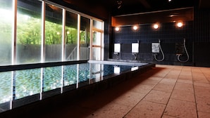 Piscina interior moderna com paredes de vidro transparente, chão de azulejo e vista para o verde lá fora.