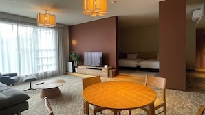 Quarto de hotel moderno com uma mesa de jantar redonda de madeira, um sofá, uma televisão e uma janela grande com cortinas.