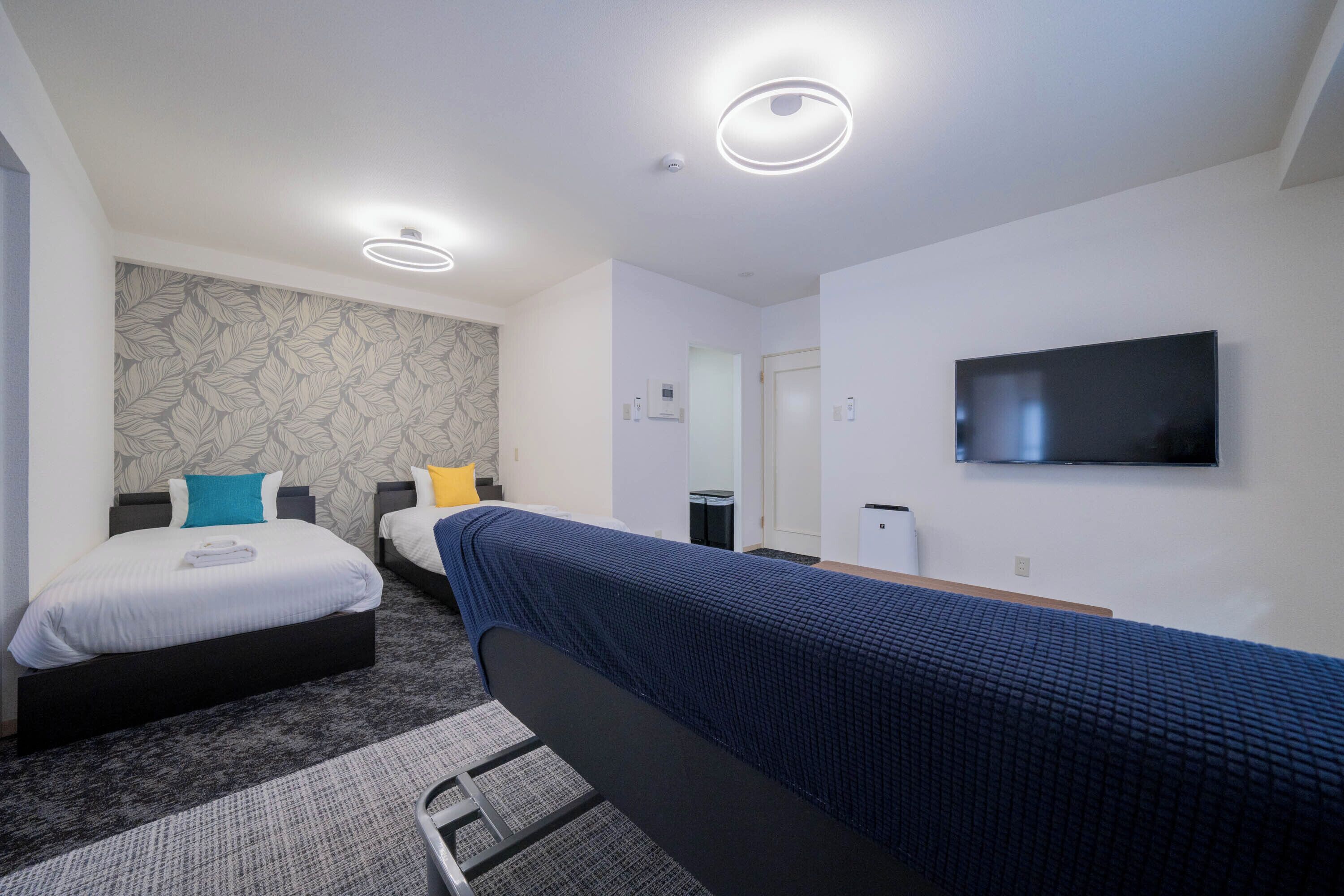 Quarto de hotel moderno com duas camas, uma televisão de tela plana e um espelho grande.