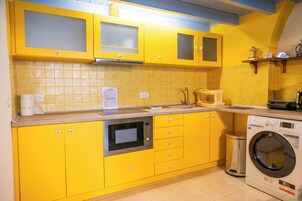 Cozinha com armários amarelos, micro-ondas, máquina de lavar e painel de azulejos.