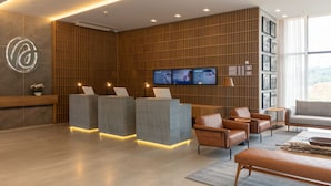 Uma área de recepção moderna com painel de madeira, balcão de atendimento, espaço de estar e uma grande janela.
