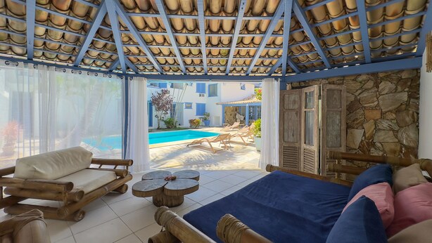 Quarto com cama, uma cadeira, uma mesa pequena e vista para a área da piscina.