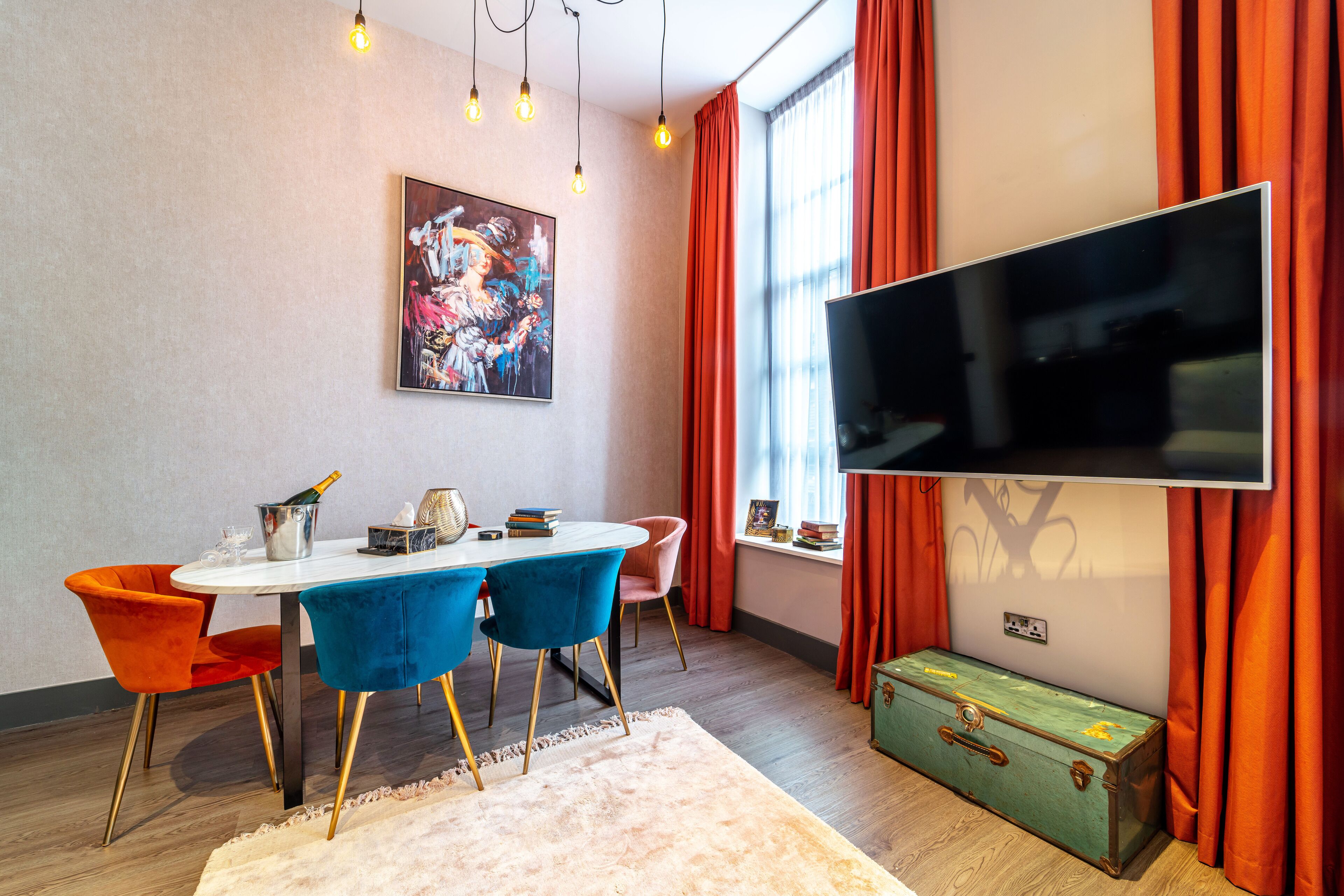 Uma sala de estar moderna com televisão de tela plana, uma mesa de jantar com cadeiras, um quadro na parede e uma janela com cortinas.