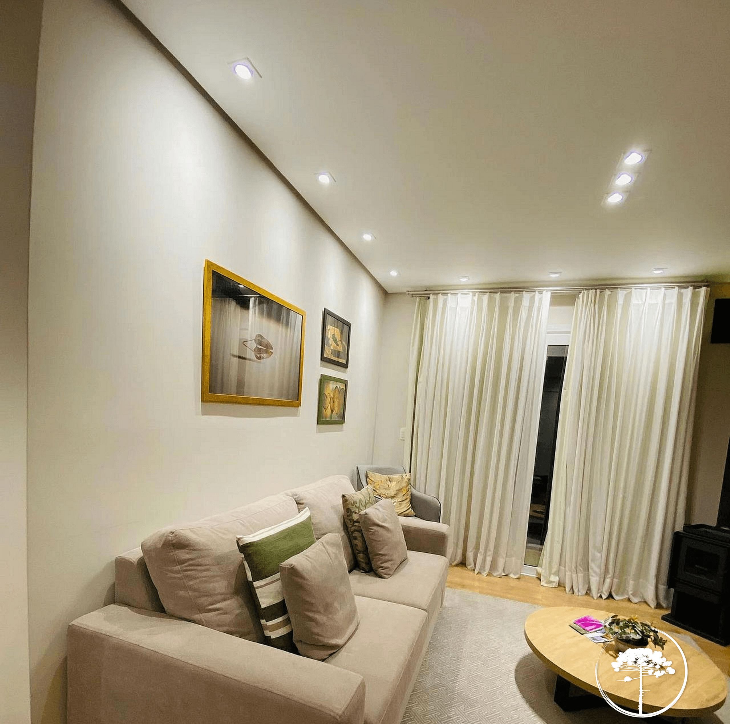 Uma sala de estar moderna com um sofá bege, uma mesa de centro e uma janela grande com cortinas leves.
