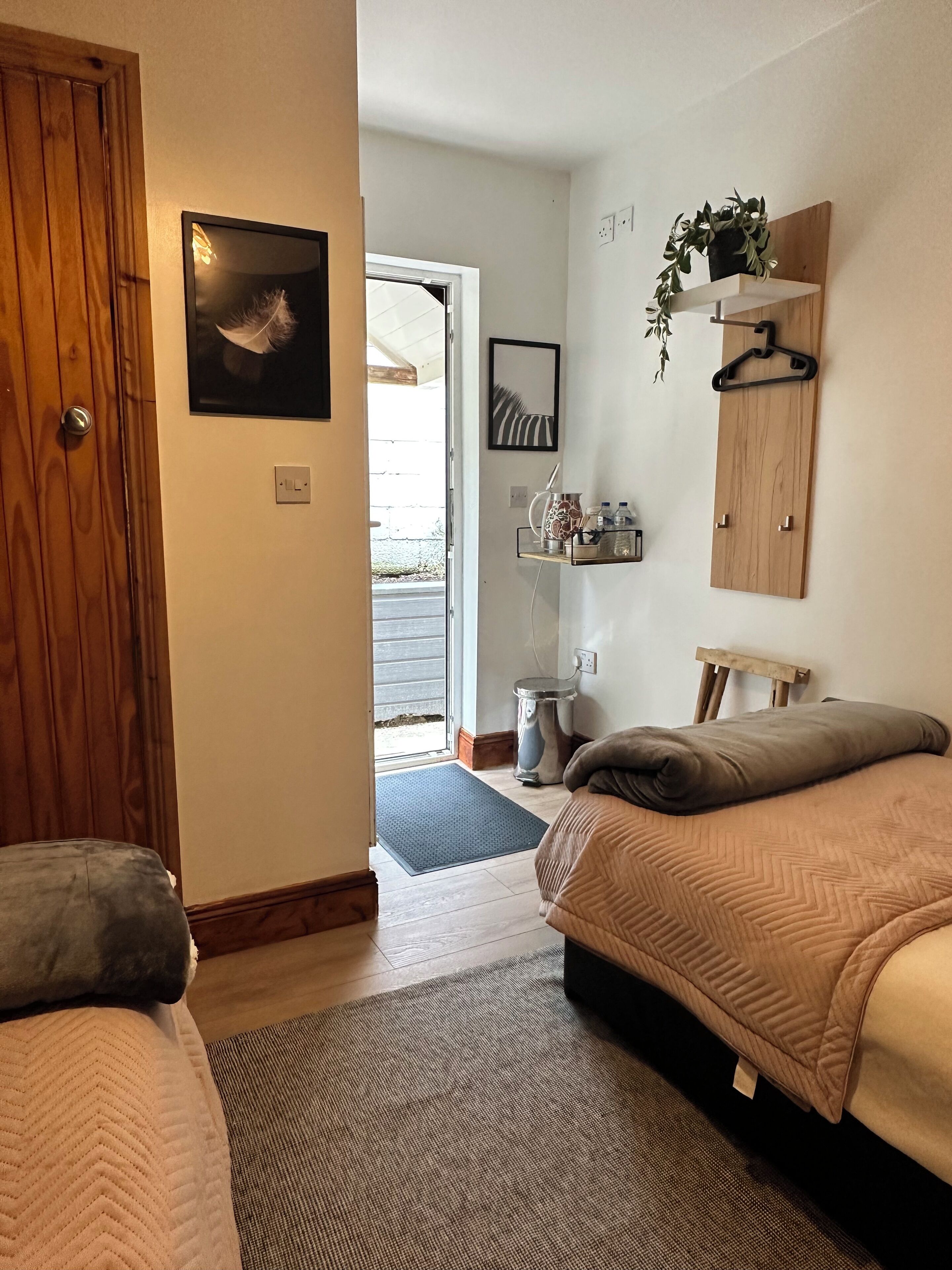 Quarto com duas camas, porta de madeira, quadro pendurado na parede, prateleira pequena com artigos de higiene pessoal e vista através de uma porta aberta.