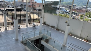 Um terraço amplo no telhado, com guarda-corpo de vidro, mobiliário para áreas externas e plantas em vasos.