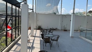 Terraço no telhado com mesa e cadeiras, plantas em vasos e vista para a paisagem urbana.
