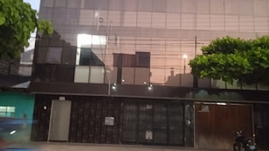 Um edifício moderno com fachada de vidro, uma pequena entrada com porta de madeira e uma motocicleta estacionada na frente.