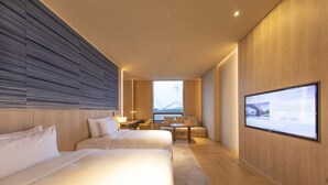 Quarto de hotel moderno com duas camas, uma escrivaninha, uma cadeira e uma grande tela de televisão.
