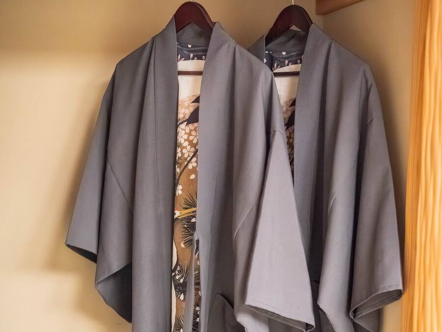 Duas vestes cinzentas penduradas em um cabide de madeira em frente a uma parede bege.