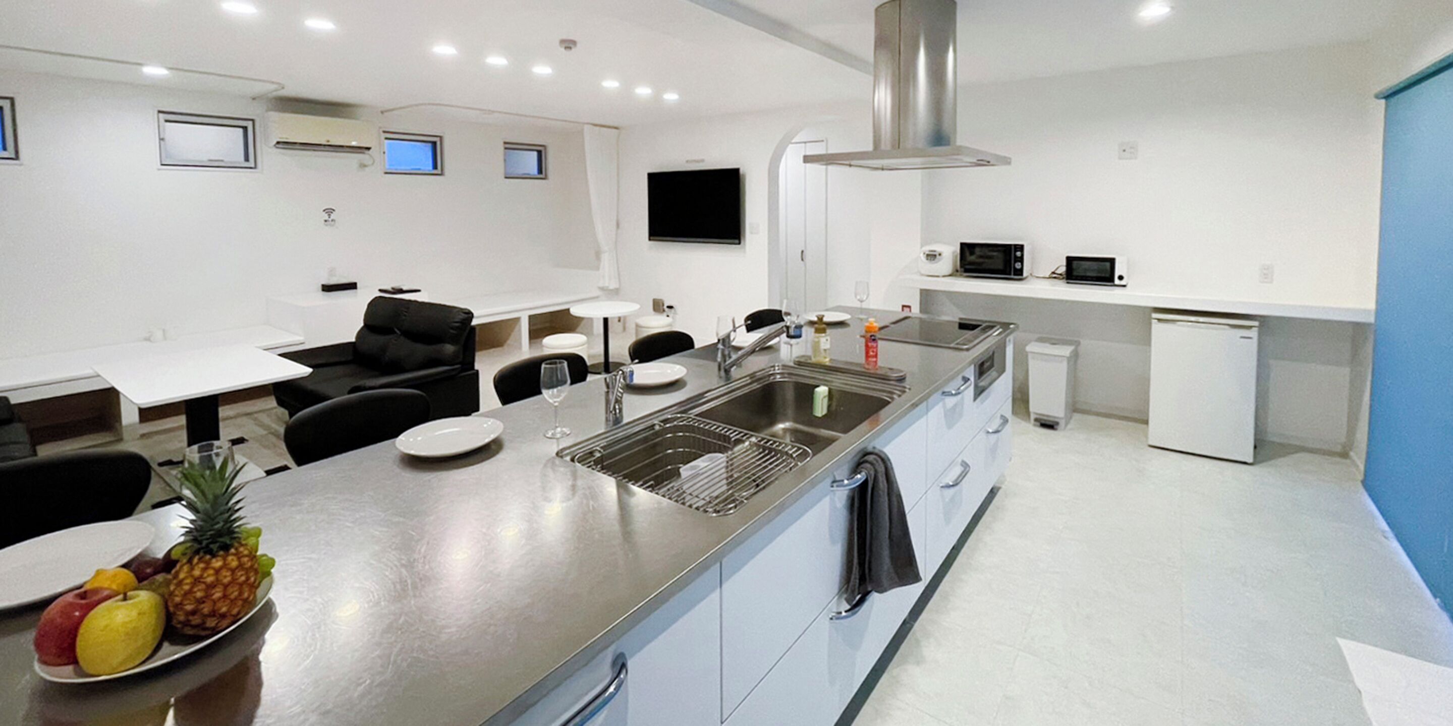 Uma cozinha moderna com ilha central, micro-ondas embutido e frigorífico pequeno.