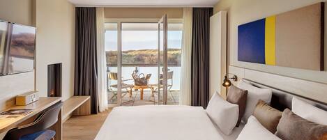 Quarto de hotel com uma cama, uma escrivaninha, uma cadeira, uma televisão, um quadro e vista para o exterior.