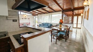 Uma cozinha com ilha central, vigas de madeira no teto e área de jantar com cadeiras e mesa.