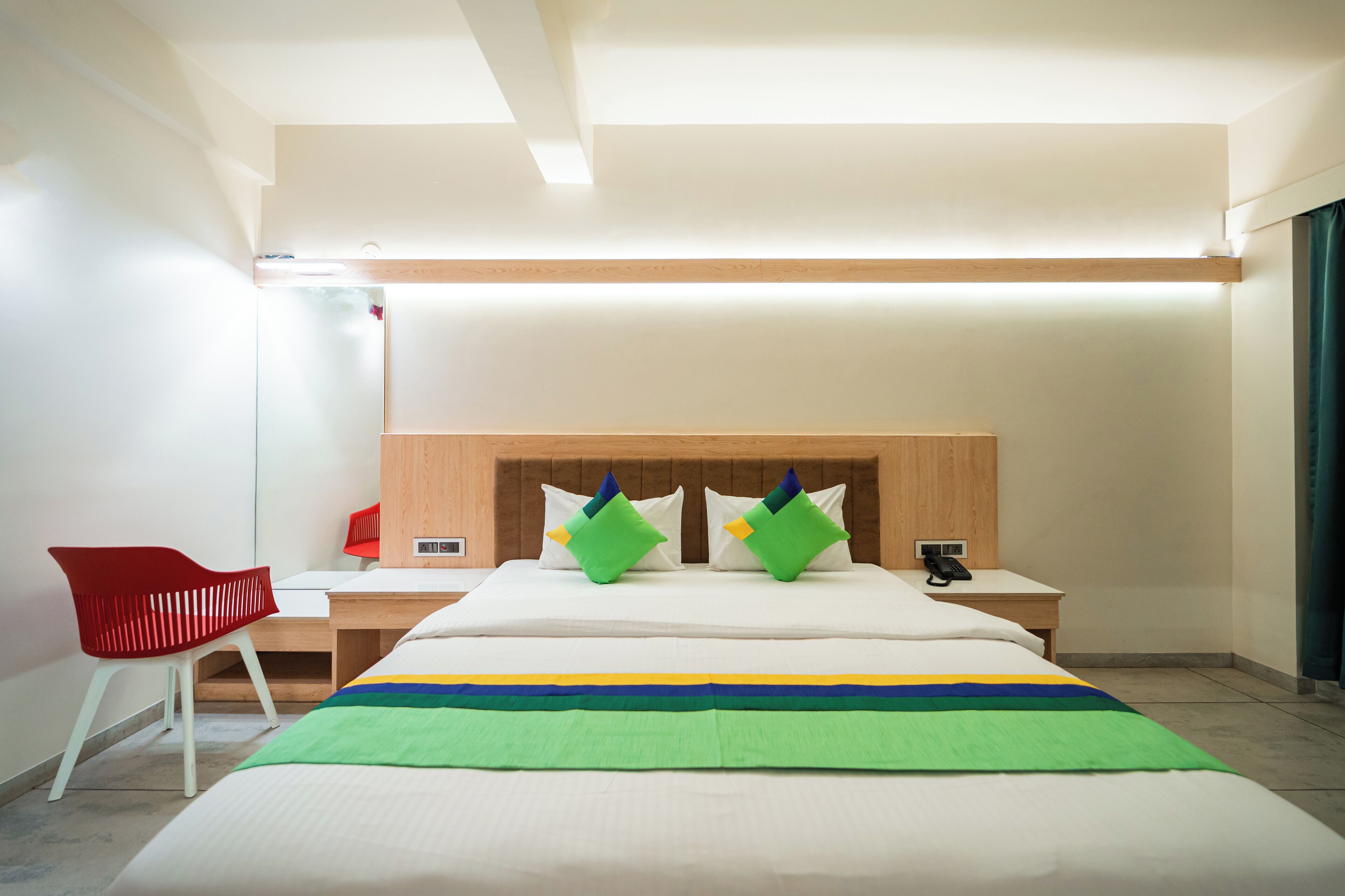 Quarto de hotel com uma cama grande, cabeceira de madeira, escrivaninha com cadeira e telefone.