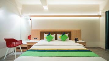 Quarto de hotel com uma cama grande, cabeceira de madeira, escrivaninha com cadeira e telefone.